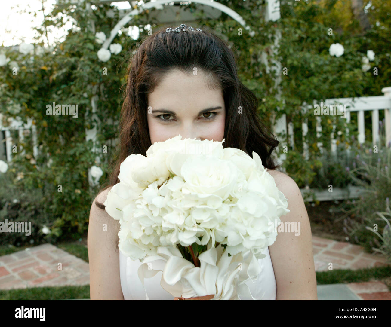 Bride holding flower bouquet front of her face in garden , portrait ...