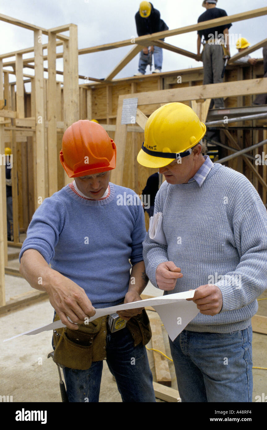 construction workers looking at plans while other builders working on ...