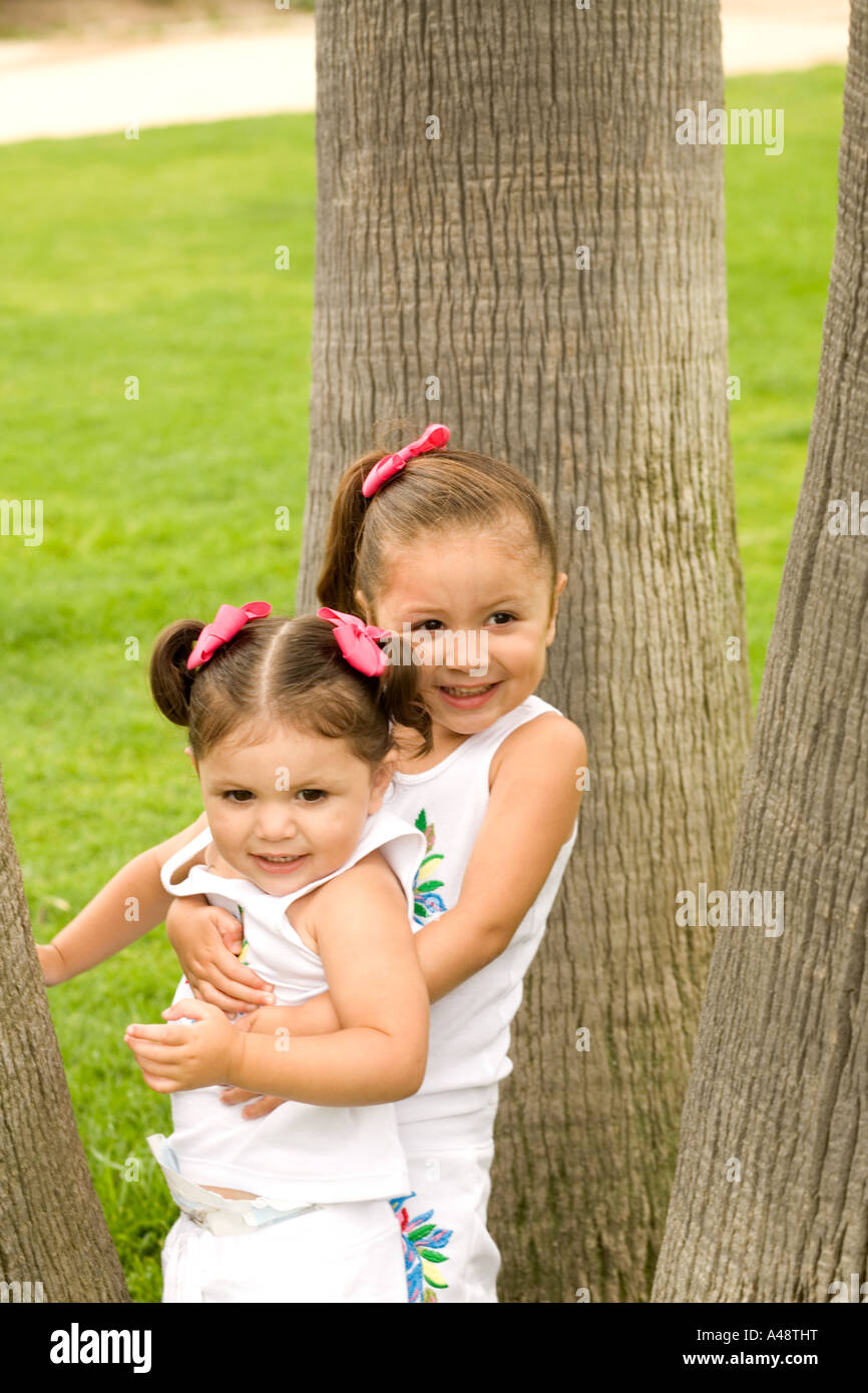 Girls (2-3) standing by tree trunk, smiling Stock Photo - Alamy