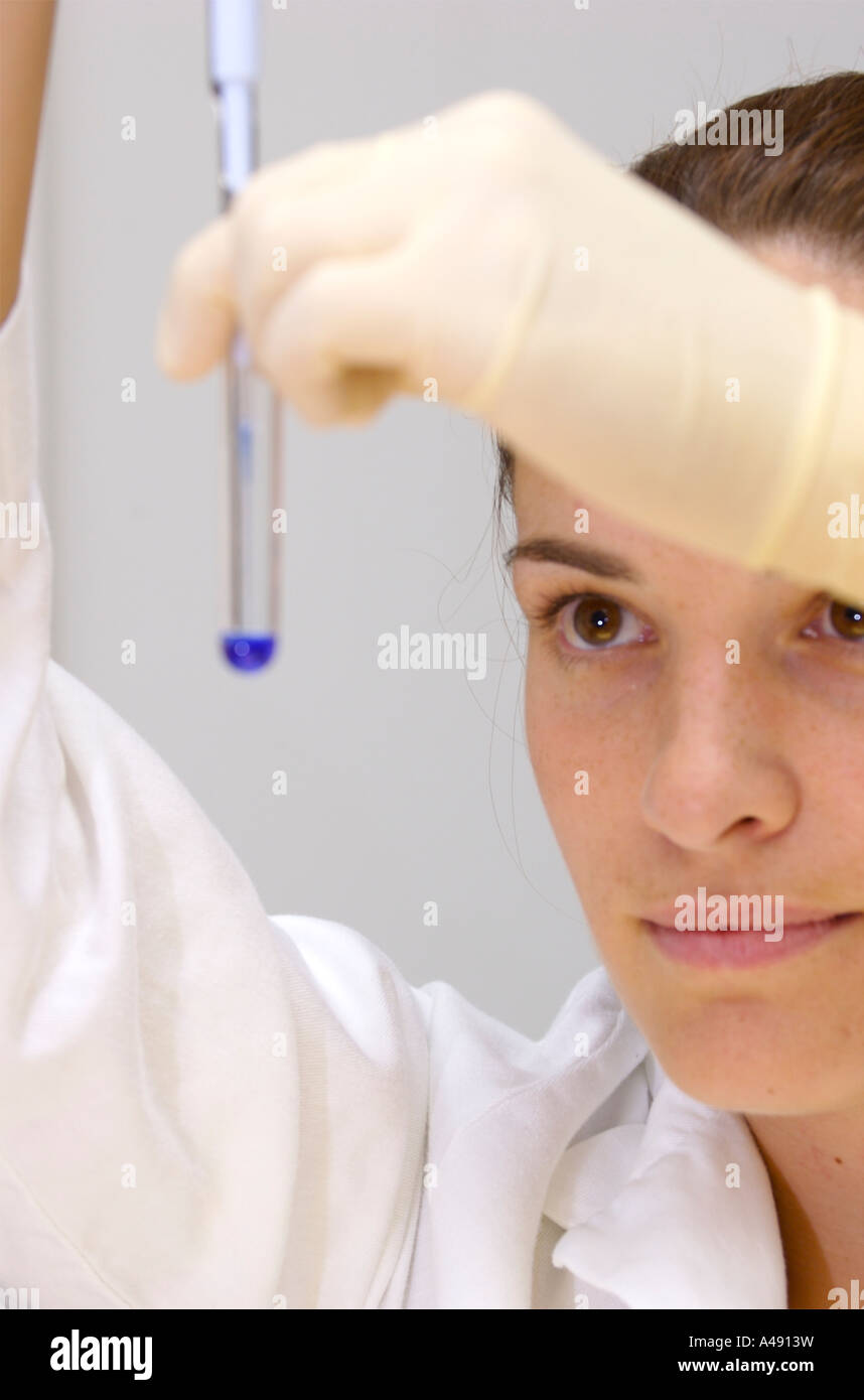 A female scientist wearing a white laboratory coat intently examines a ...