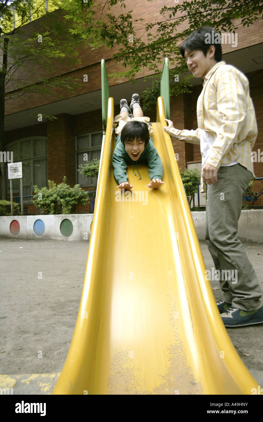 Low angle view of a boy sliding on a slide with his father standing ...