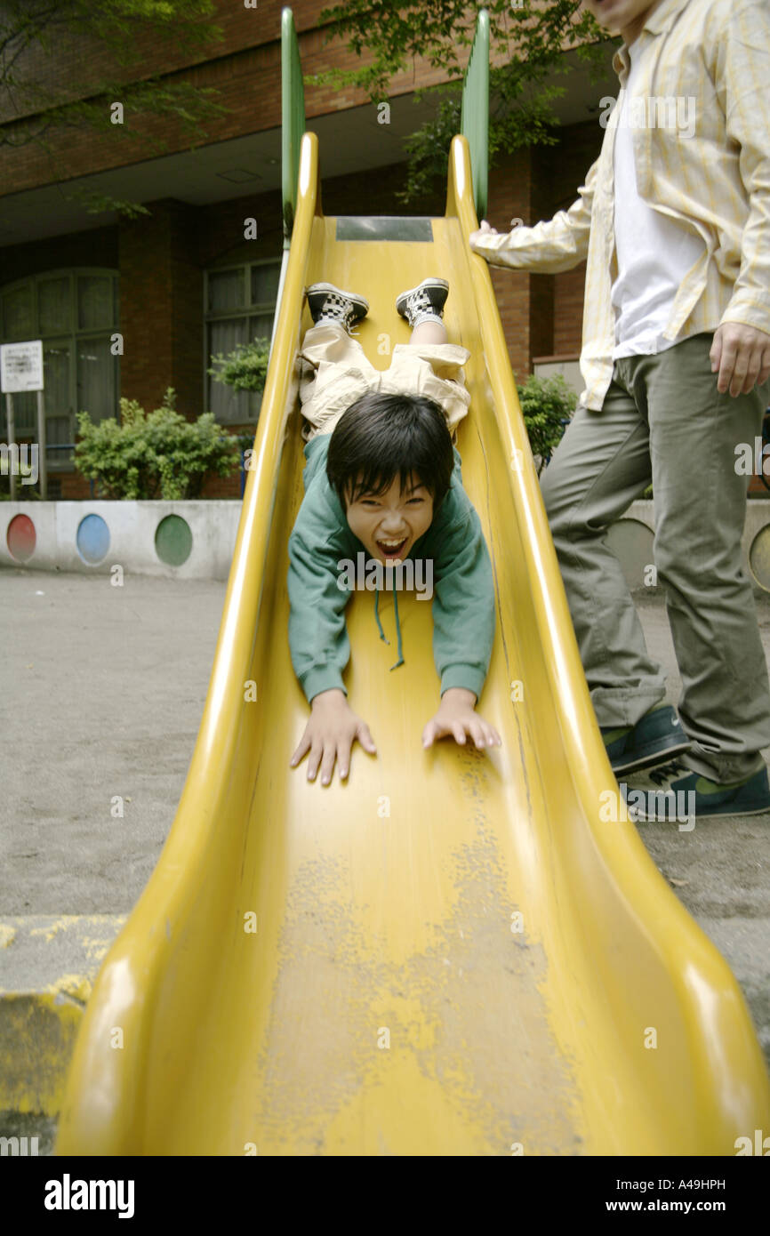 Low angle view of a boy sliding on a slide with his father standing ...