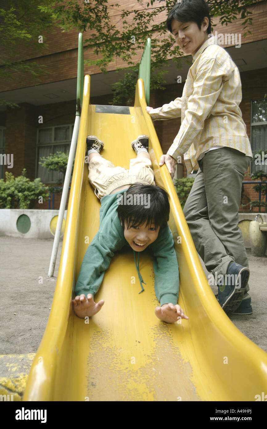 Low angle view of a boy sliding on a slide with his father standing ...