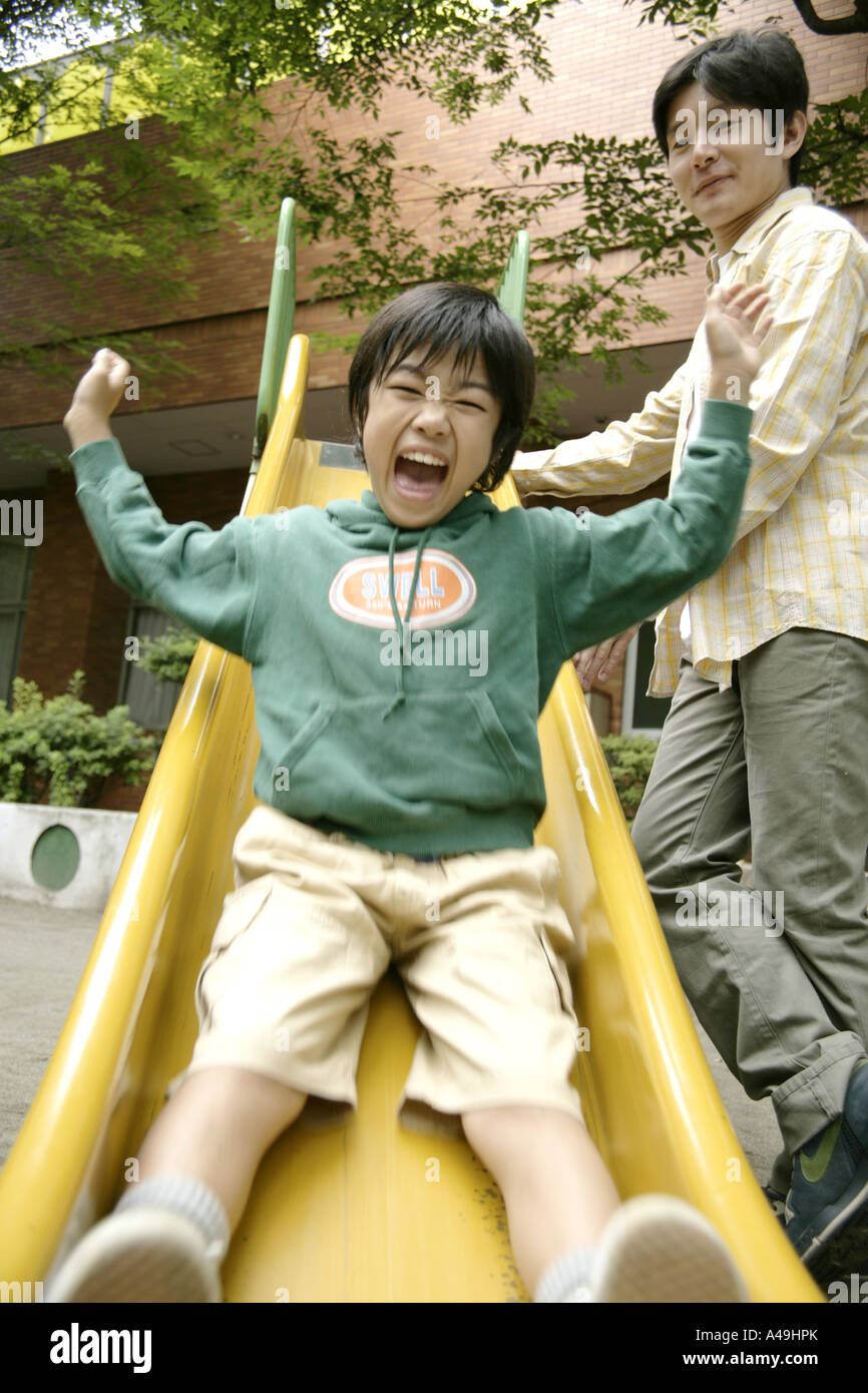 Low angle view of a boy sliding on a slide with his father standing ...