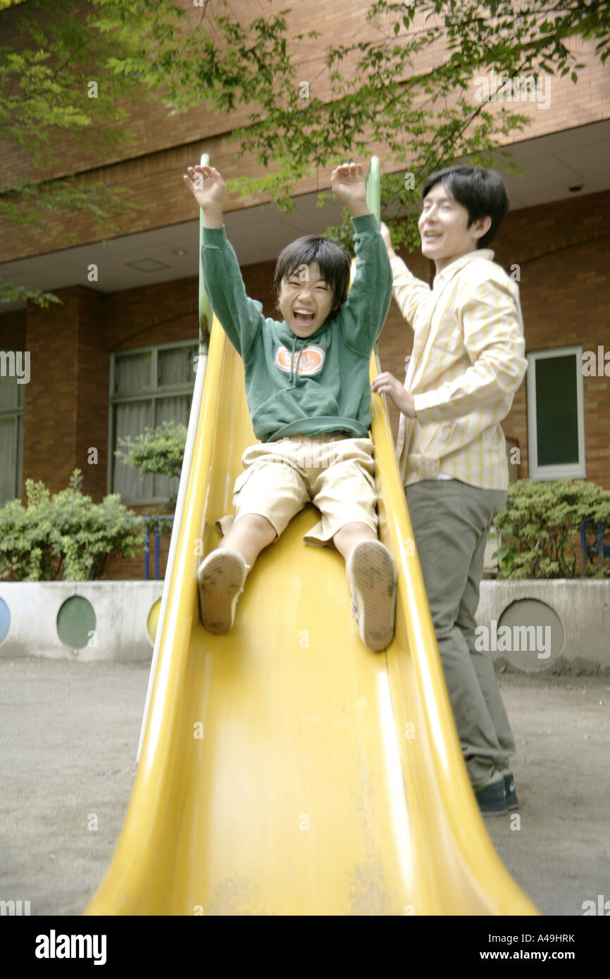 Low angle view of a boy sliding on a slide with his father standing ...