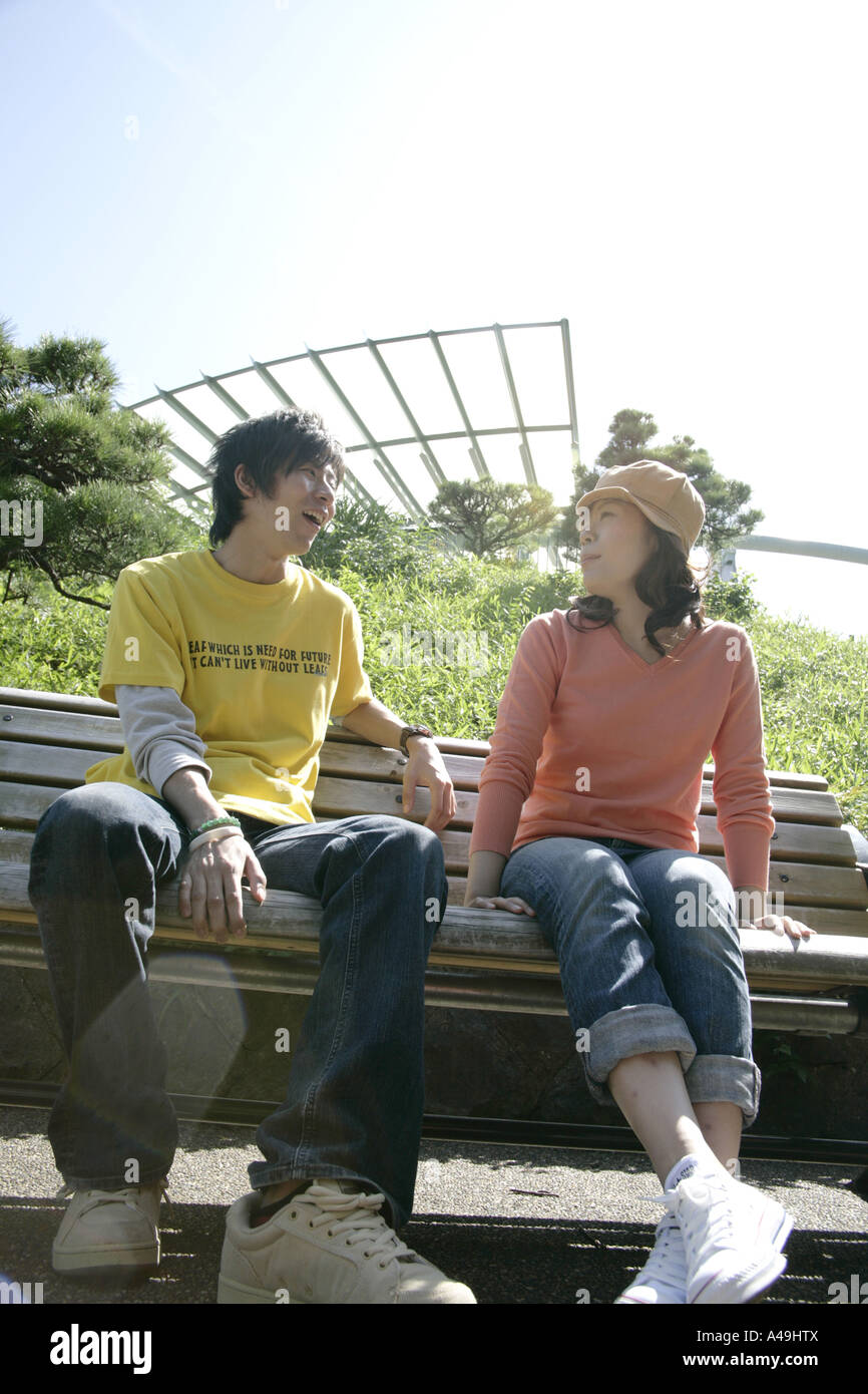 Low angle view of a young couple sitting on a park bench and smiling ...