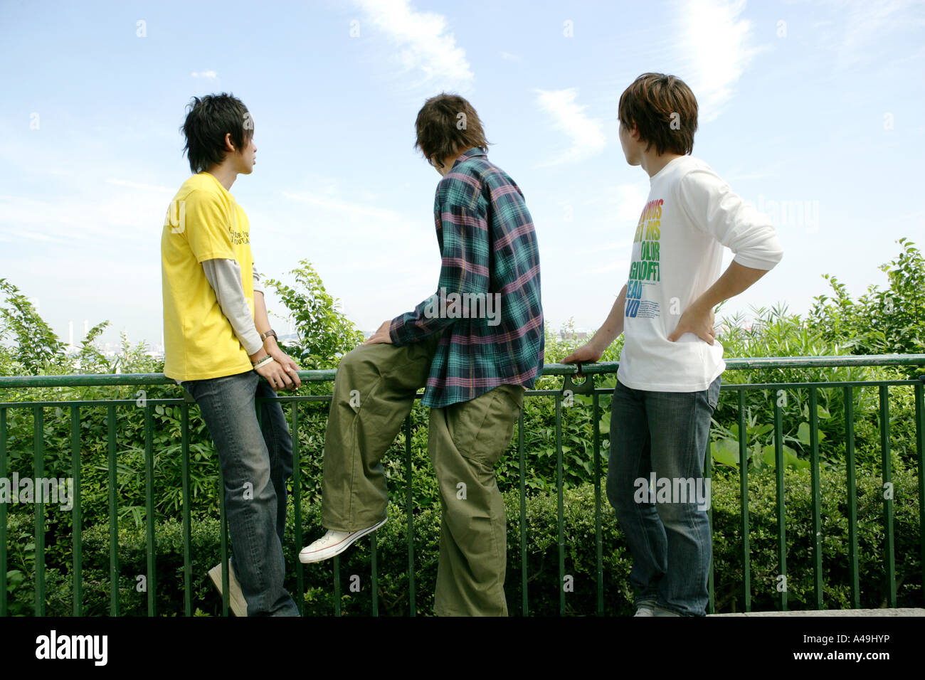Side profile of two men sitting on a railing with another man standing ...