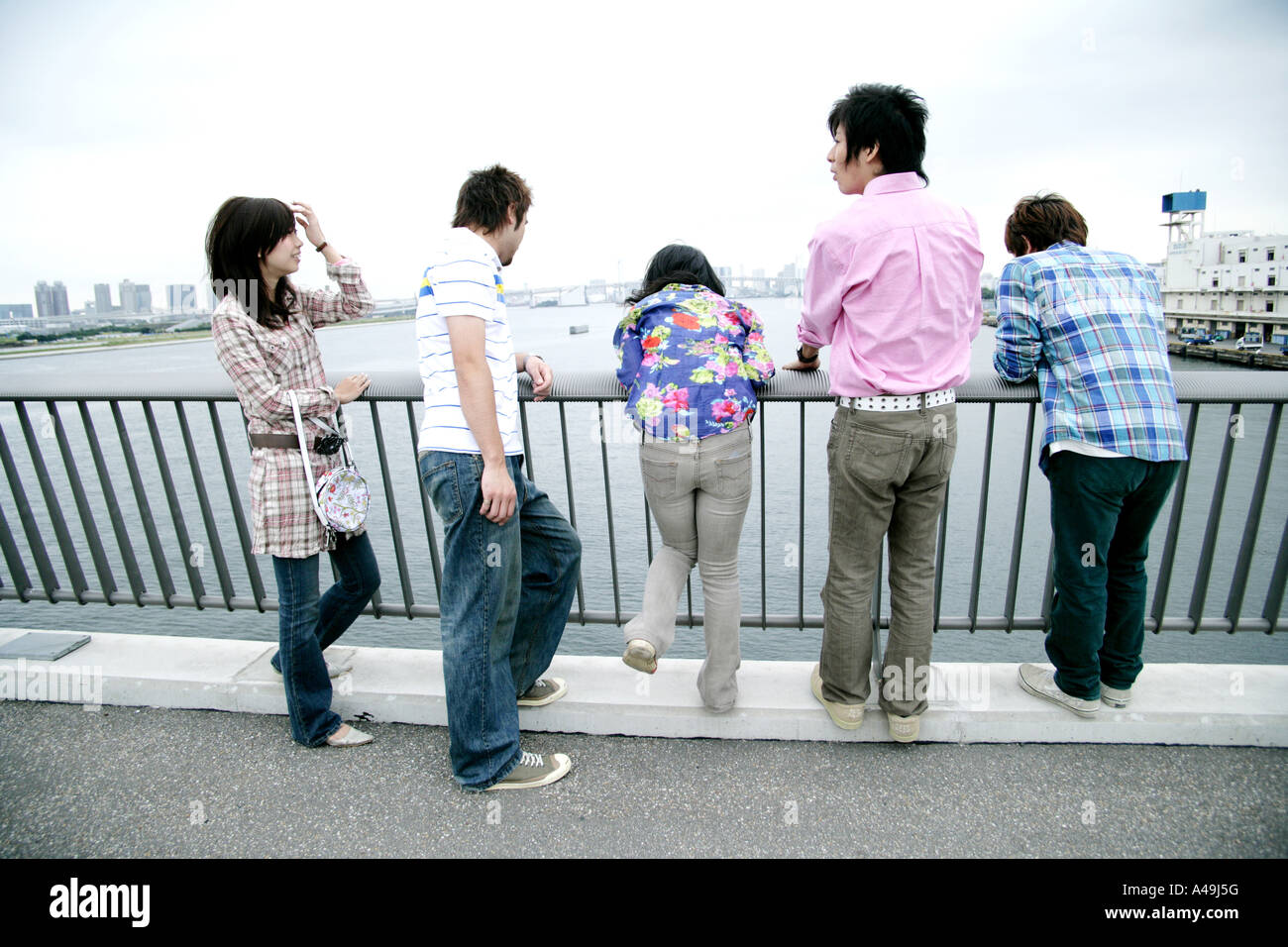Three young men and two young women leaning against a railing Stock ...