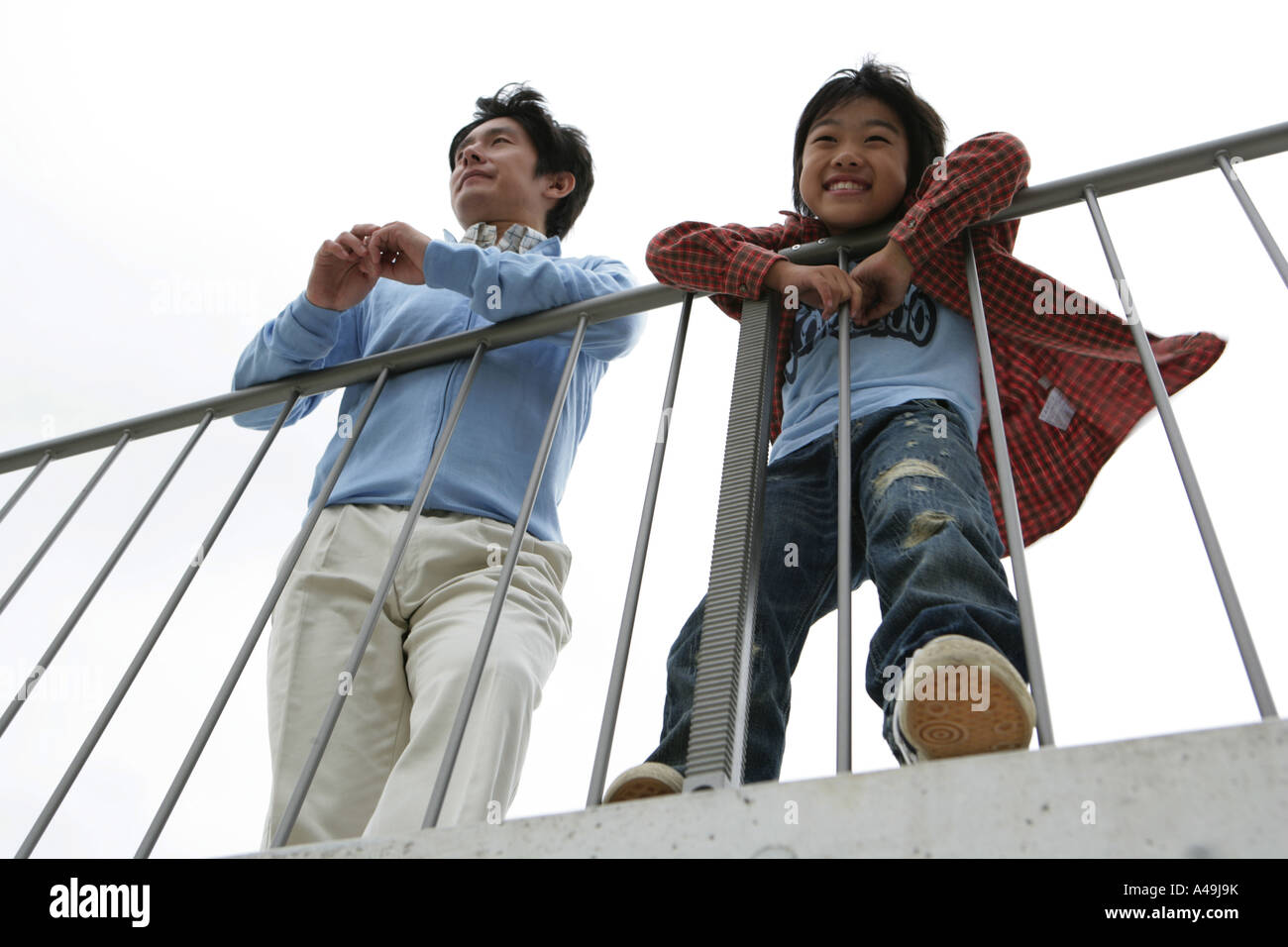 Low angle view of a mid adult man and his son leaning against a railing ...
