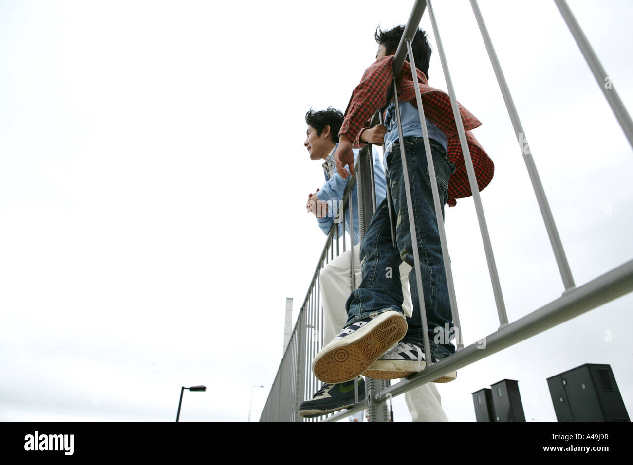 Low angle view of a mid adult man and his son leaning against a railing ...