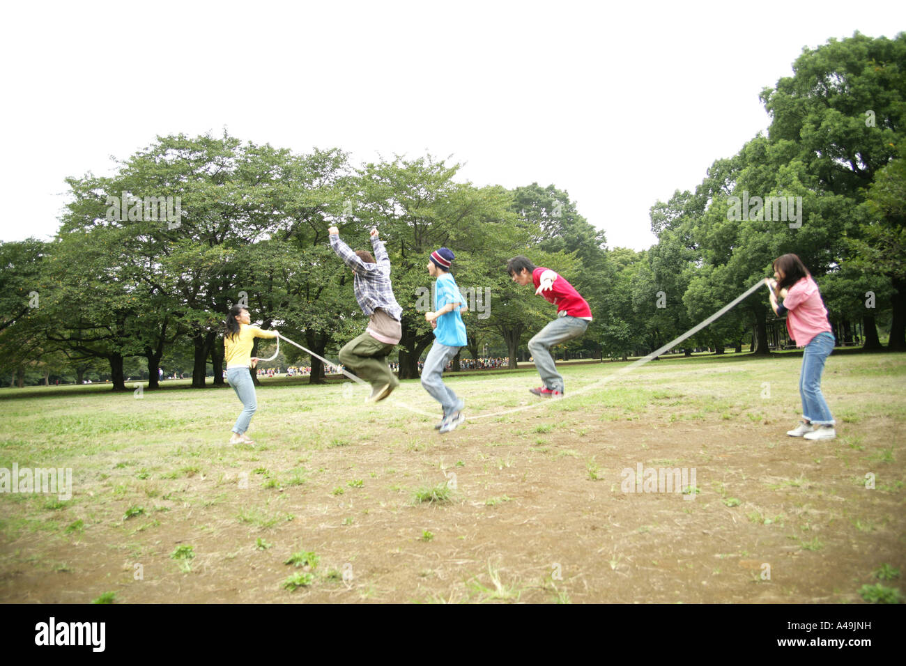 Three young men and two young women playing jump rope Stock Photo - Alamy