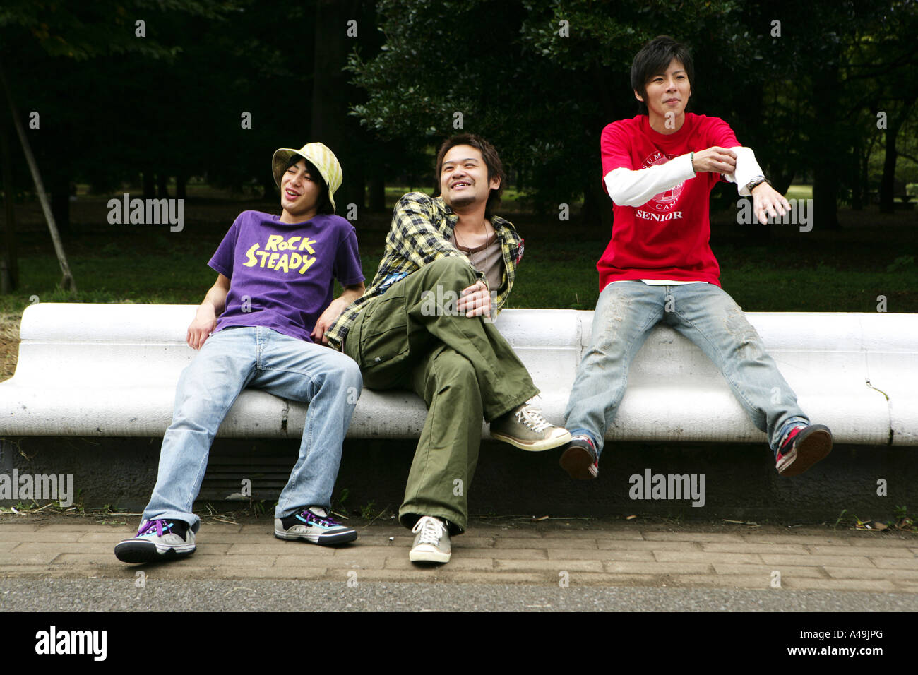 Three young men sitting on a park bench Stock Photo - Alamy