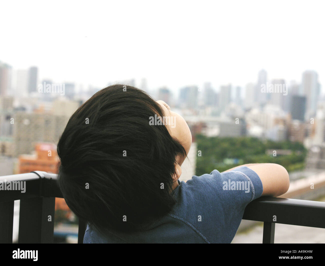 Rear view of a boy standing and leaning on a railing Stock Photo - Alamy