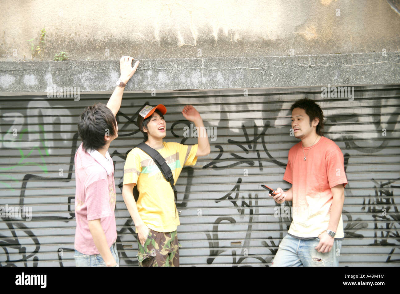 Three young men standing together in front of a wall Stock Photo - Alamy
