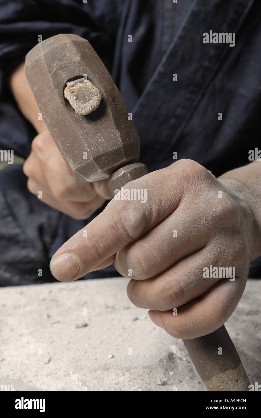 Close up of a person s hand using a chisel and a hammer on a stone ...