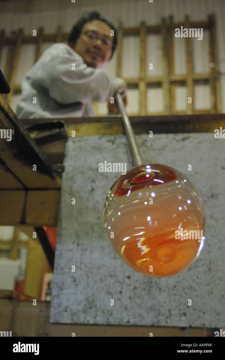 Low angle view of a mid adult man blowing molten glass with a blow pipe ...