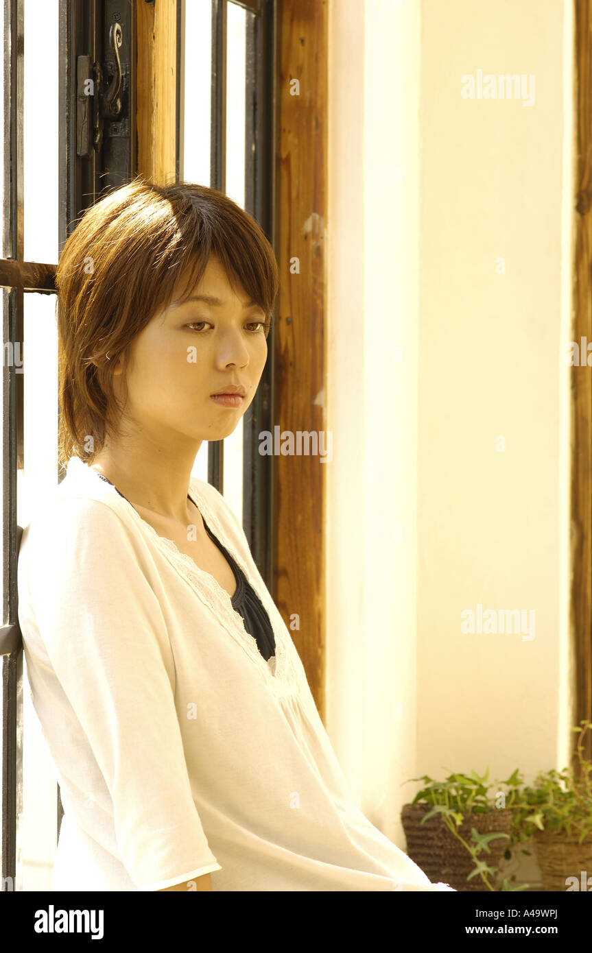 Close up of a young woman leaning against a window and looking away ...