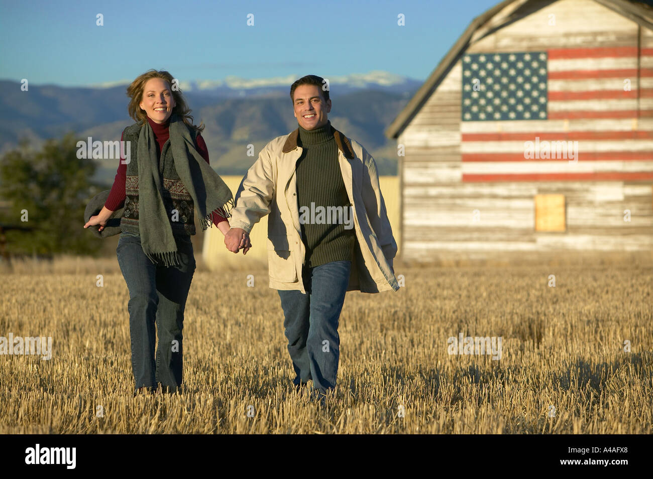 Man and woman walking through cut grass fields in Fall with barn and ...