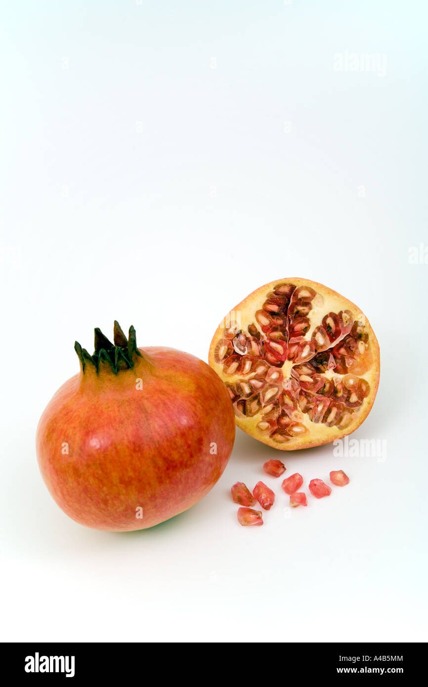Two pomegranates, one split open with seeds exposed on a white ...