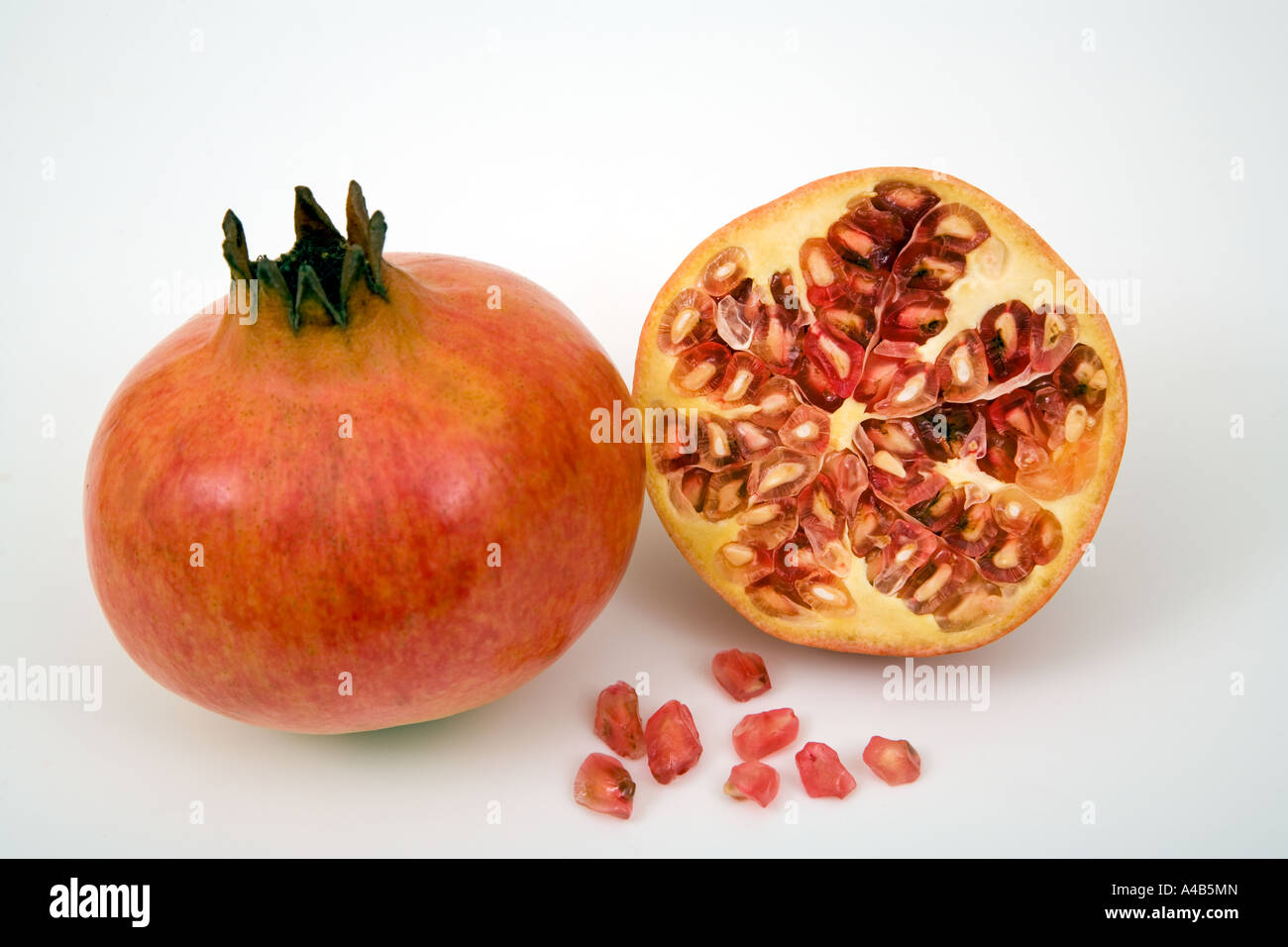 Two pomegranates, one split open with seeds exposed on a white ...