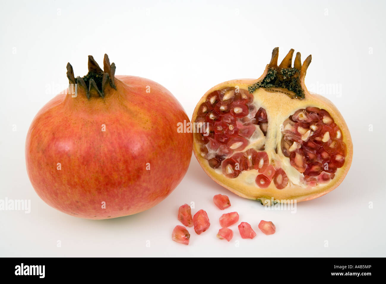 Two pomegranates, one split open with seeds exposed on a white ...