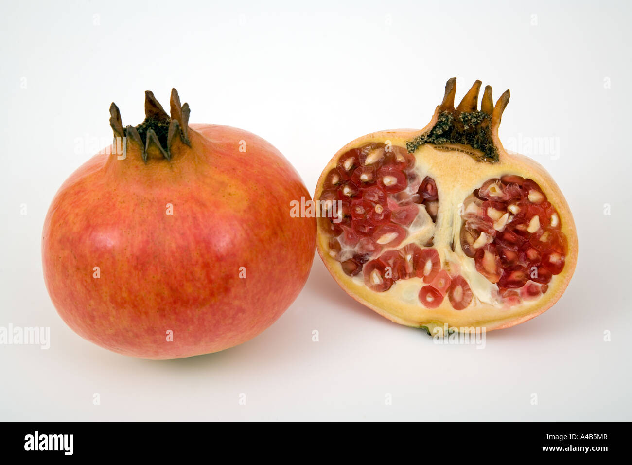 Two pomegranates, one split open with seeds exposed on a white ...