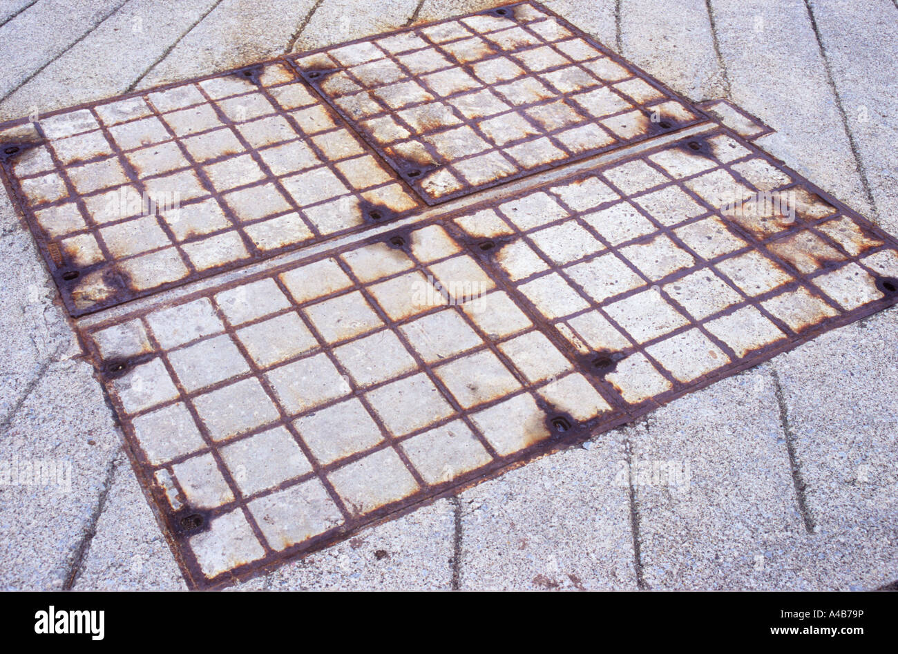 Close up of a grid of four large square iron and cement manhole covers ...
