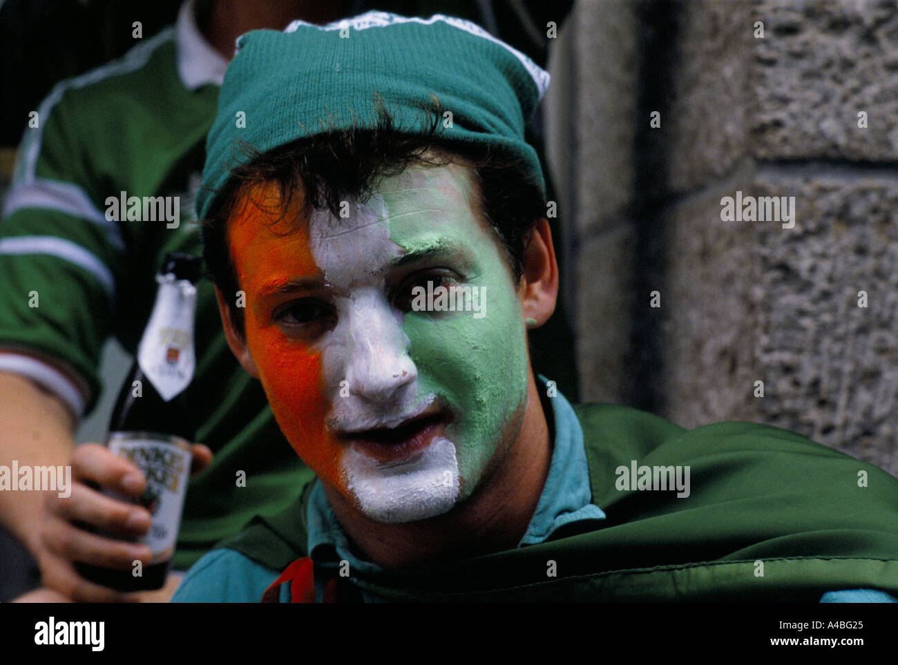 An Irish football fan, his face painted with the Irish tricolor drinks ...