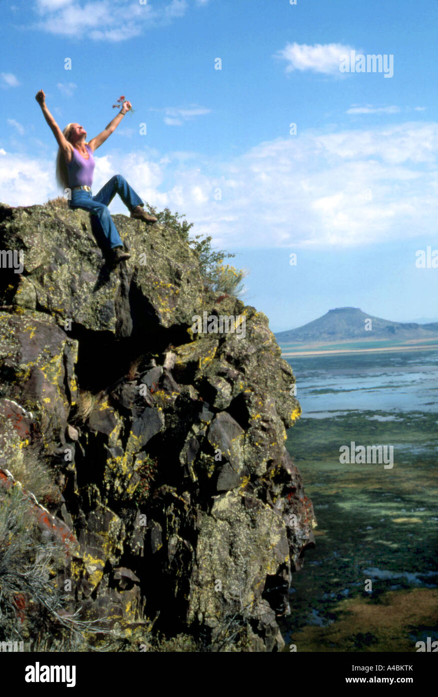 Woman on a high rock cliff overlooking a marsh, celebrating life and ...
