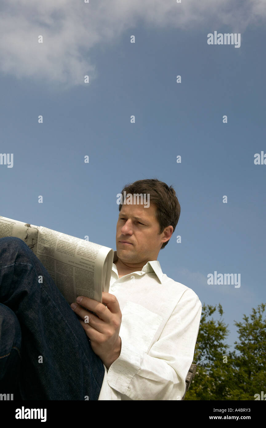Man reading newspaper in park, low angle view Stock Photo - Alamy