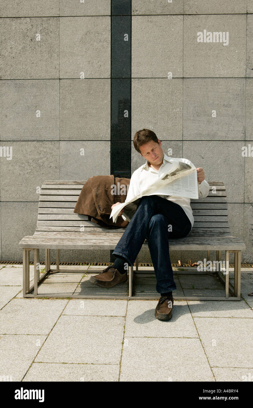 Man sitting on bench reading newspaper Stock Photo - Alamy