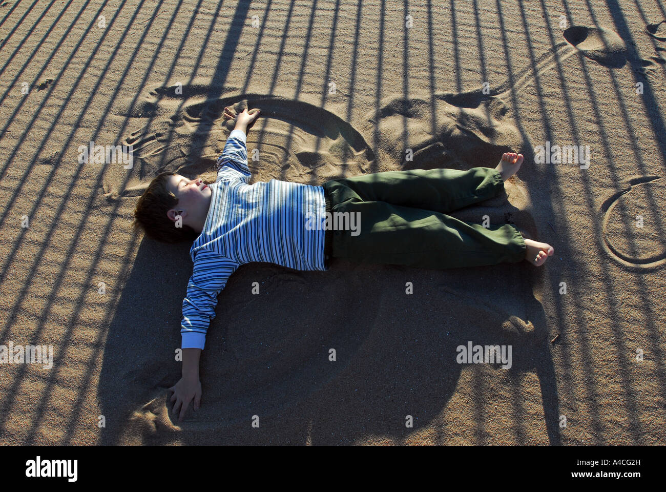 A child plays in the sand with graphic sunlight in late afternoon ...