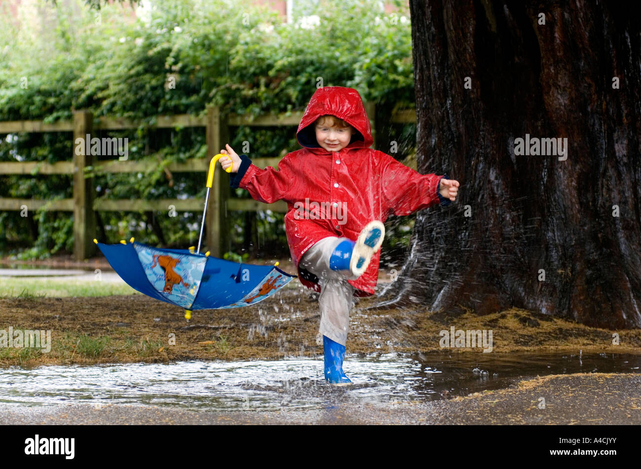 Small boy in red coat and blue umbrella splashing and having fun in a ...