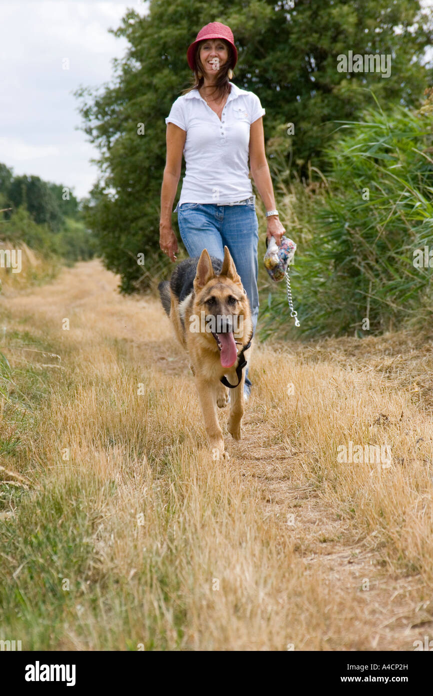 Woman walking German shepherd dog along grassy country lane Stock Photo ...