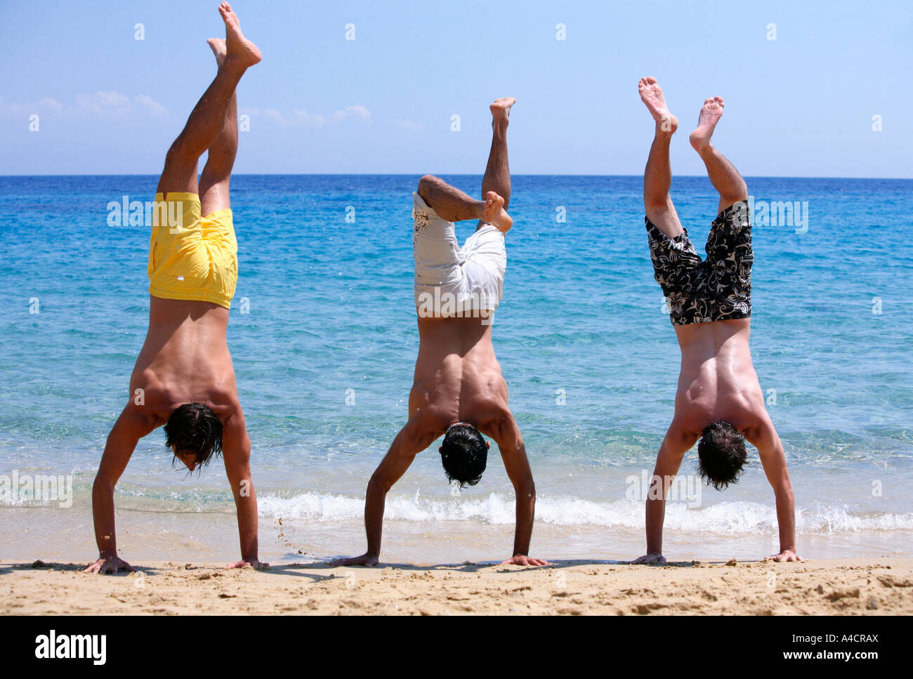 Three young men doing handstands on beach Stock Photo - Alamy