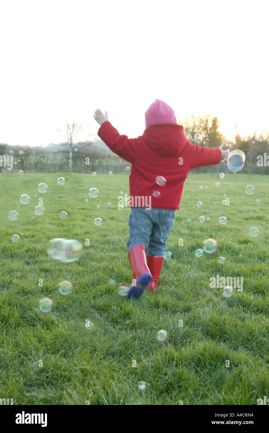Child in red coat running through area of bubbles blowing in the wind ...