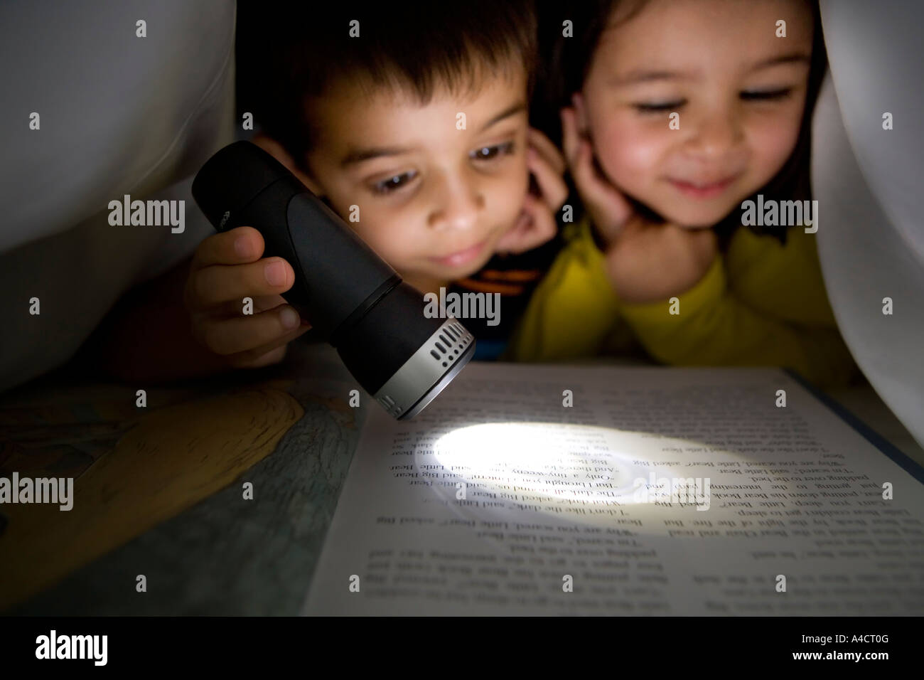 Boy and Girl read a book by torch light under the bedclothes Stock ...