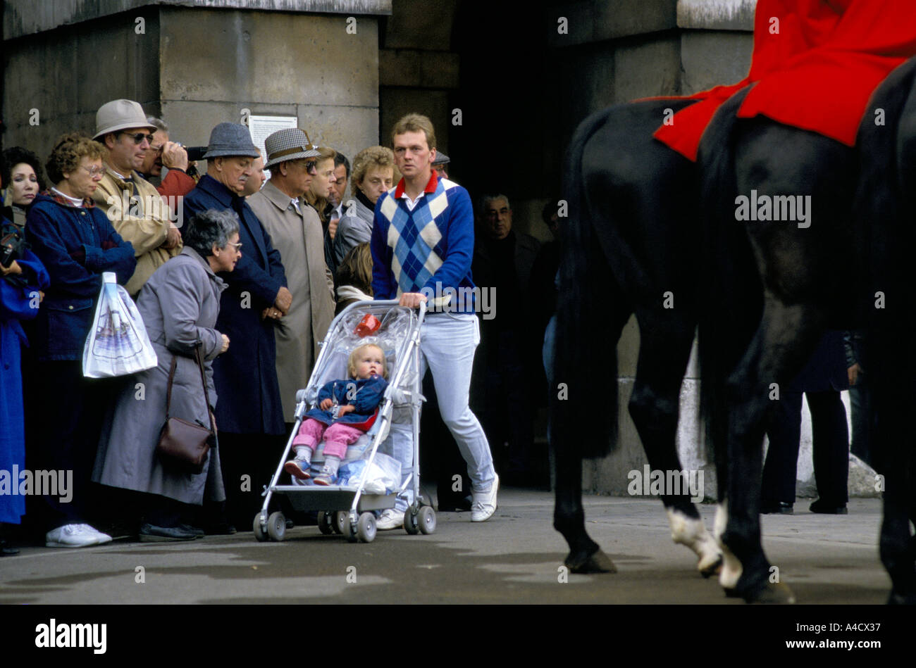 man with young child on pushchair walk pass tourists watching horse ...