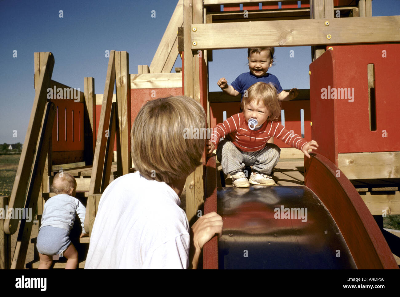 A childminder plays with toddlers on a slide in an open air playground ...