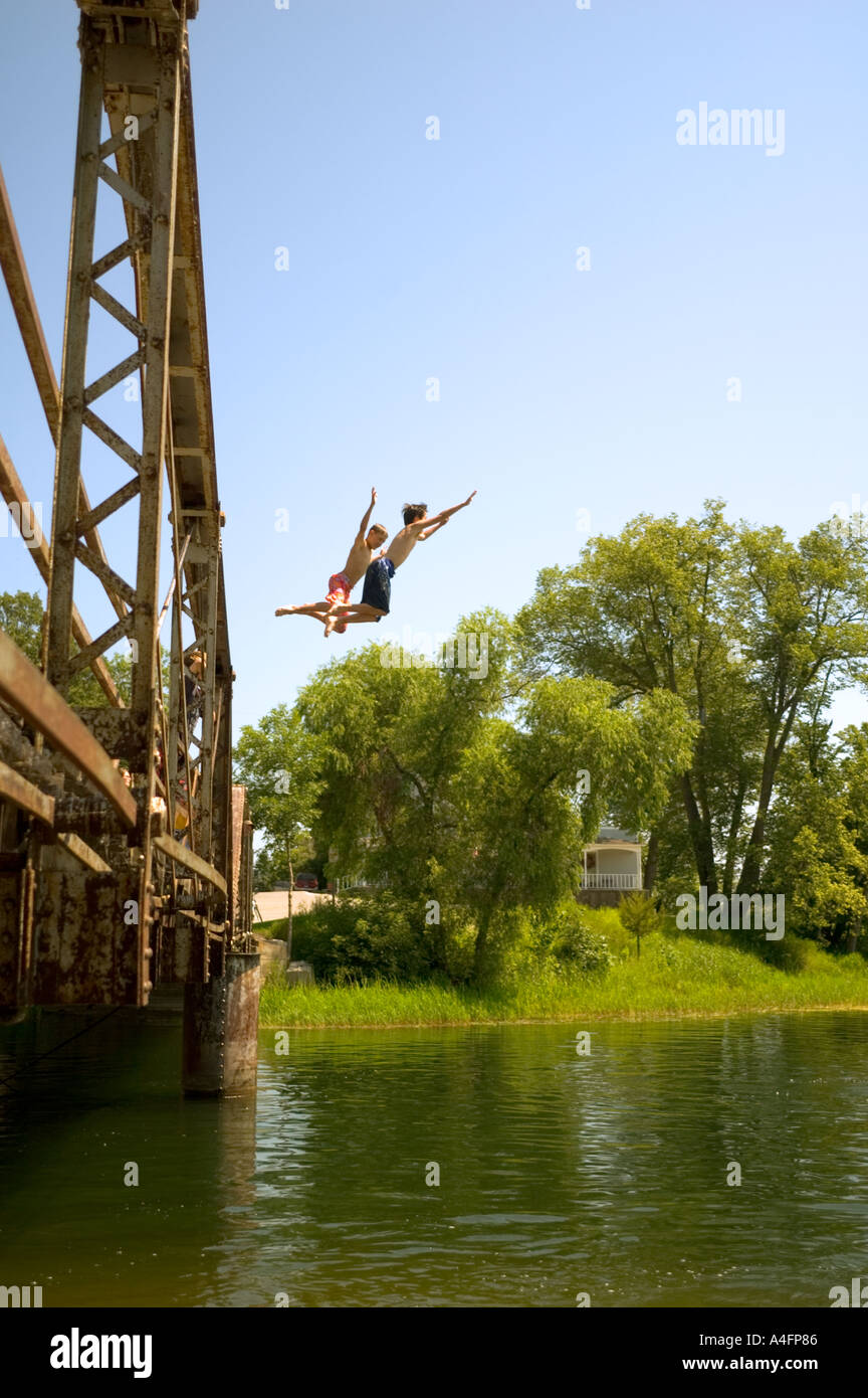 Three boys jumping off of bridge into a river Stock Photo - Alamy