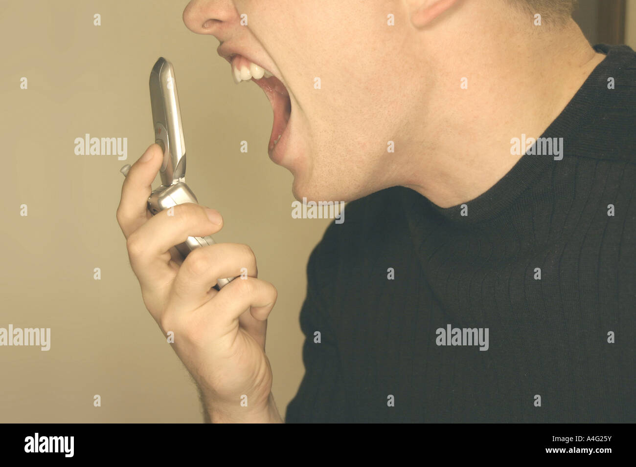 Man screaming at cell phone in black sweater and brown background Stock ...