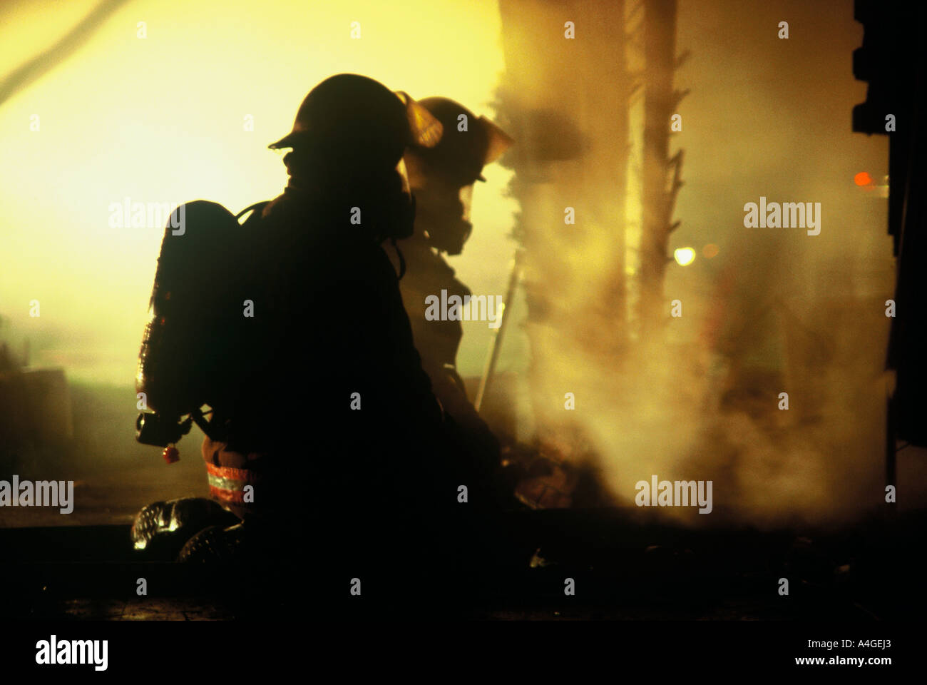 Two fire fighters kneeling in the smoke and light by front corner of ...