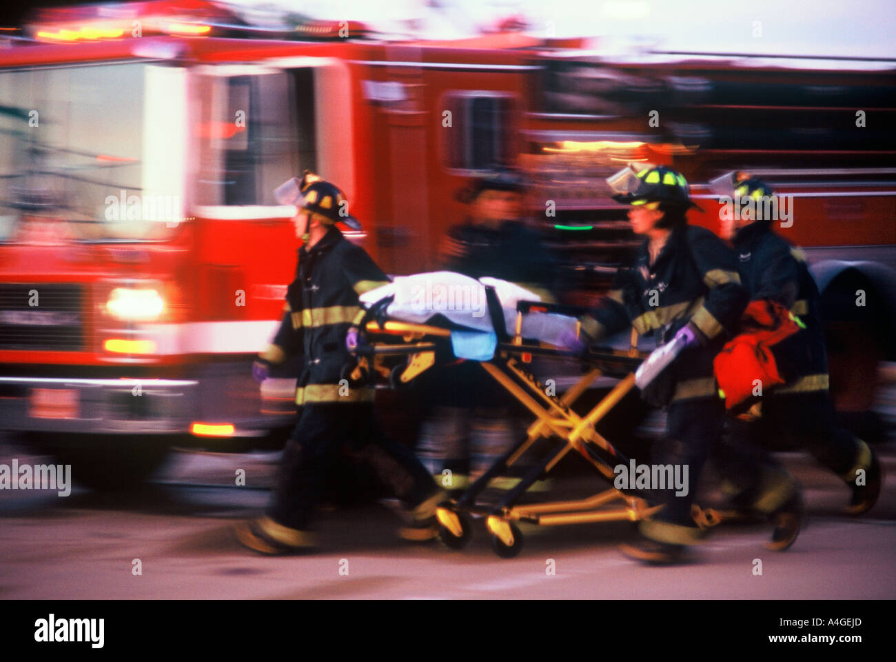 Four EMS personnel running with a cot in front of an engine at a scene ...