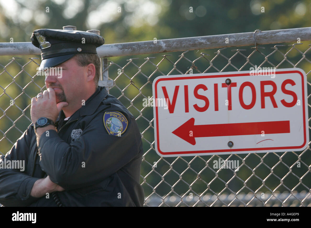 Menomonee Falls police officer at a fenced gate with a visitors sign ...