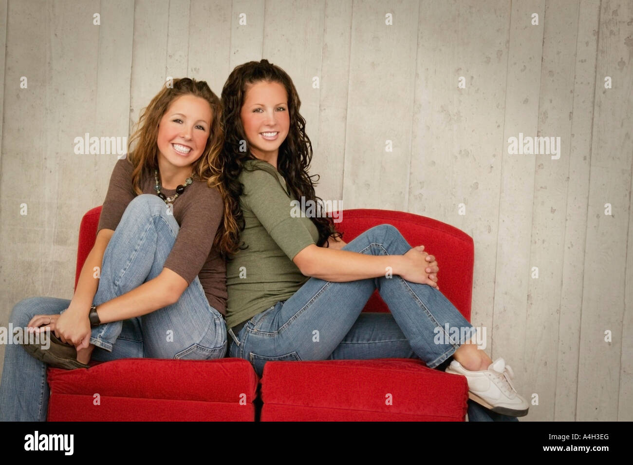 Sisters sitting back-to-back on couch Stock Photo - Alamy
