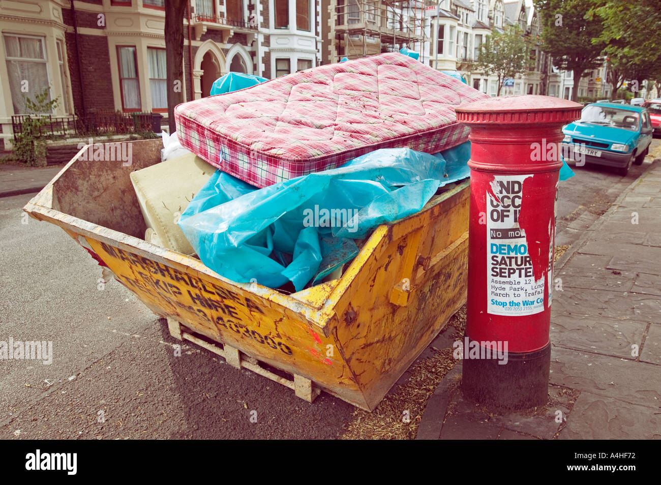 Overfull skip dumpster in road beside postbox with torn posters Cardiff ...