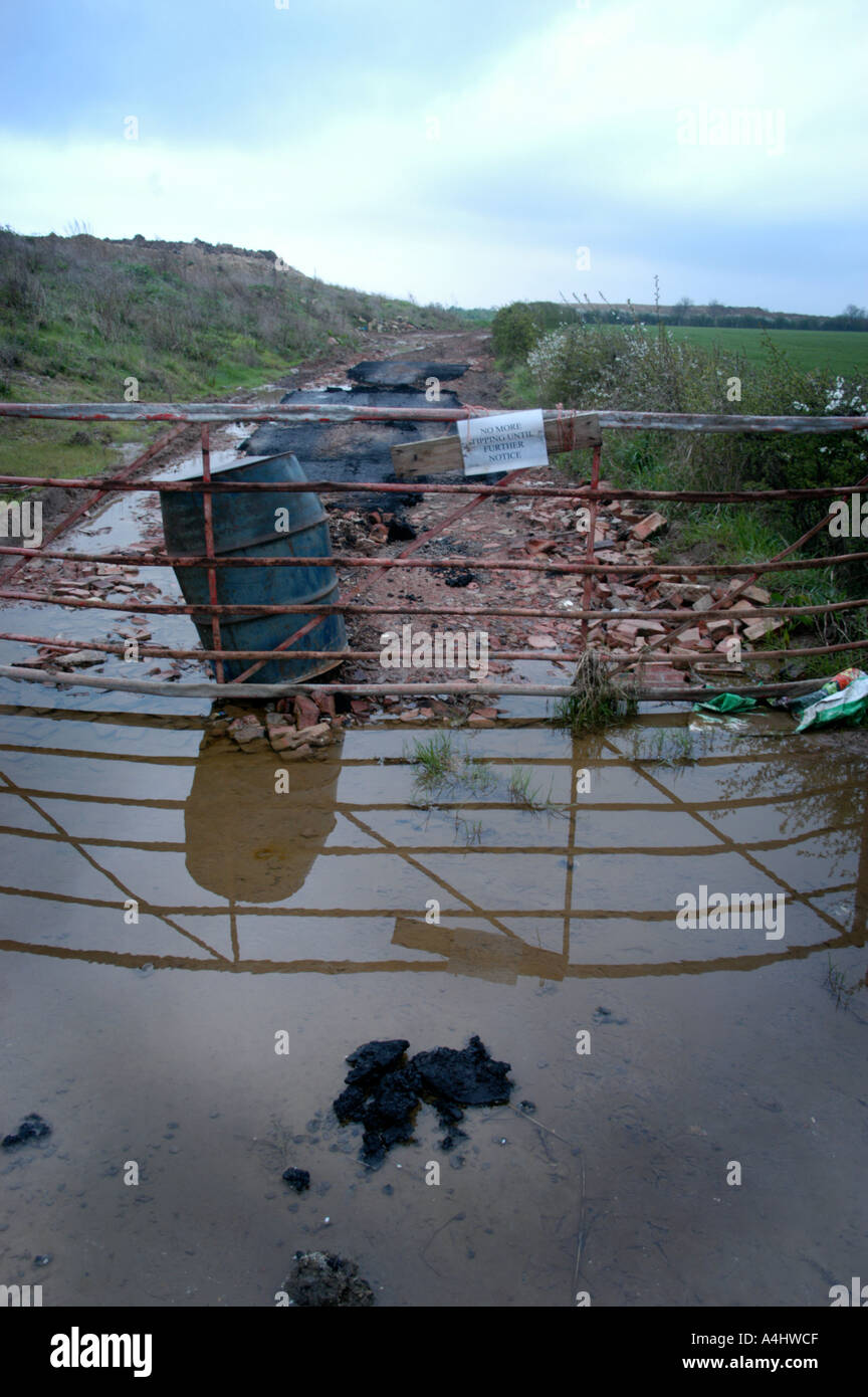 waste landfill site with oil drum and water and gate Stock Photo - Alamy