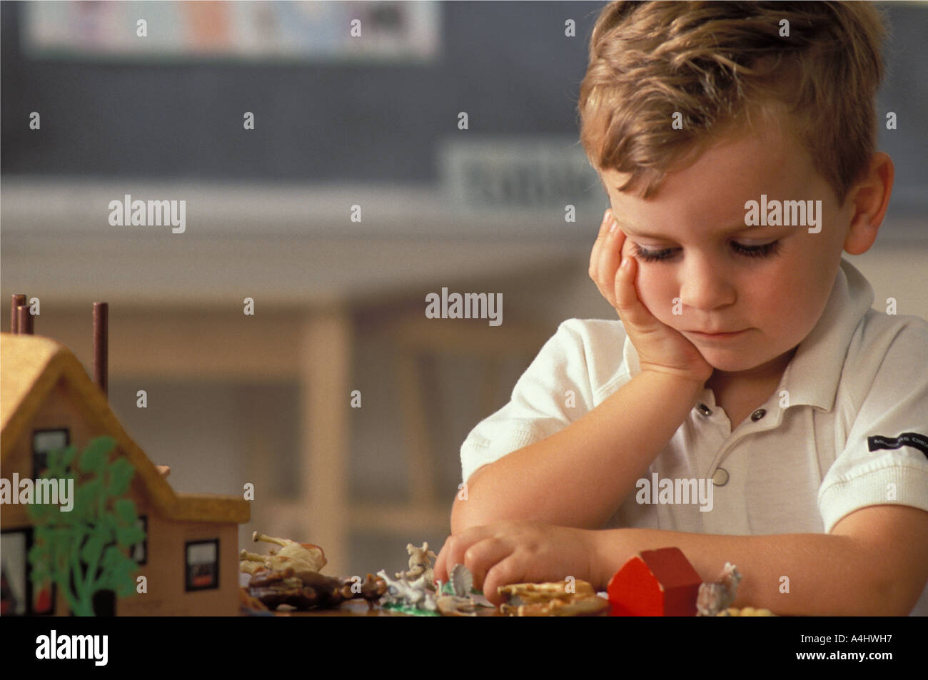 Sad looking Caucasian preschool male student playing with toy in class ...