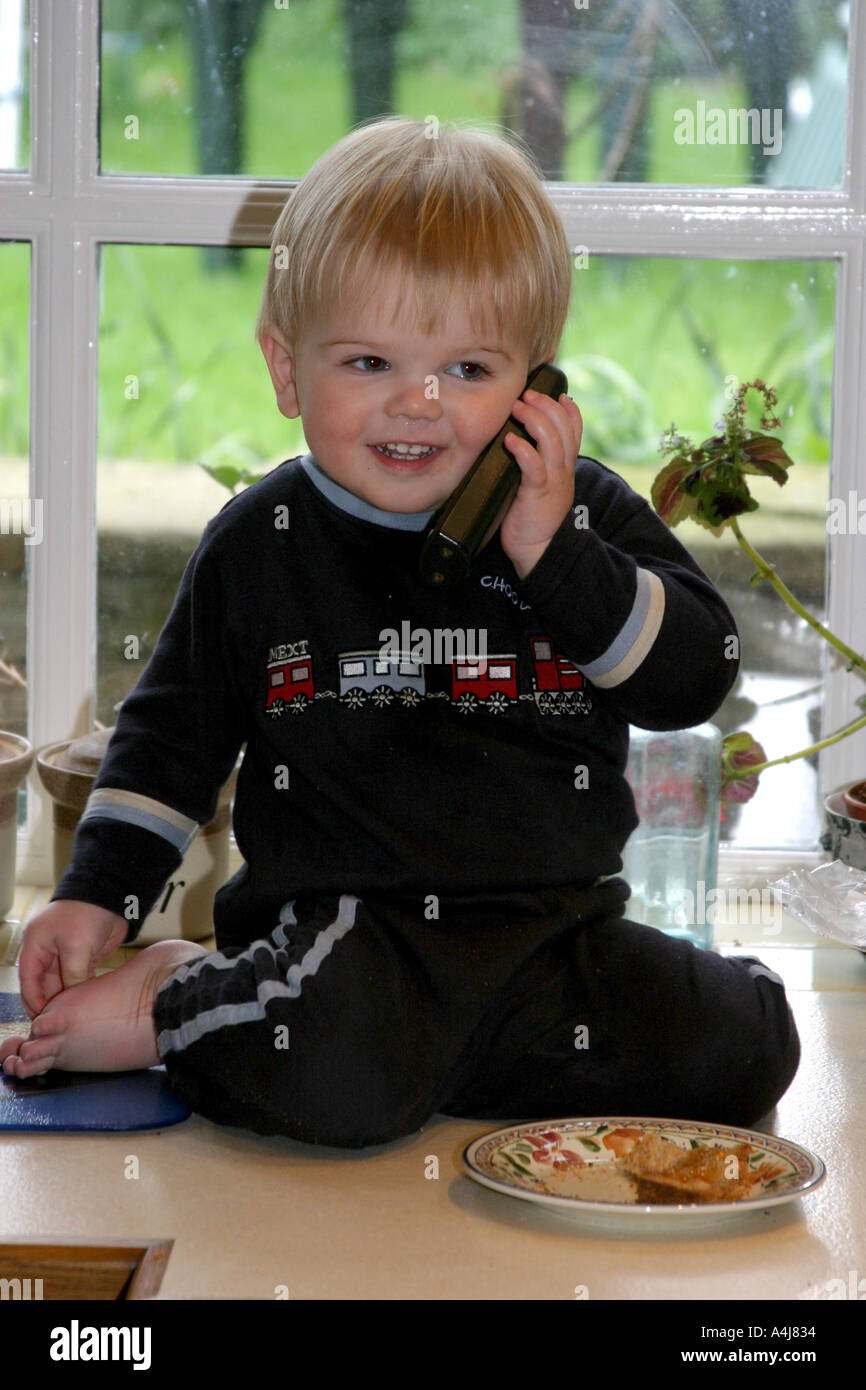 Small smiling boy child talking on cordless telephone sat on a kitchen ...