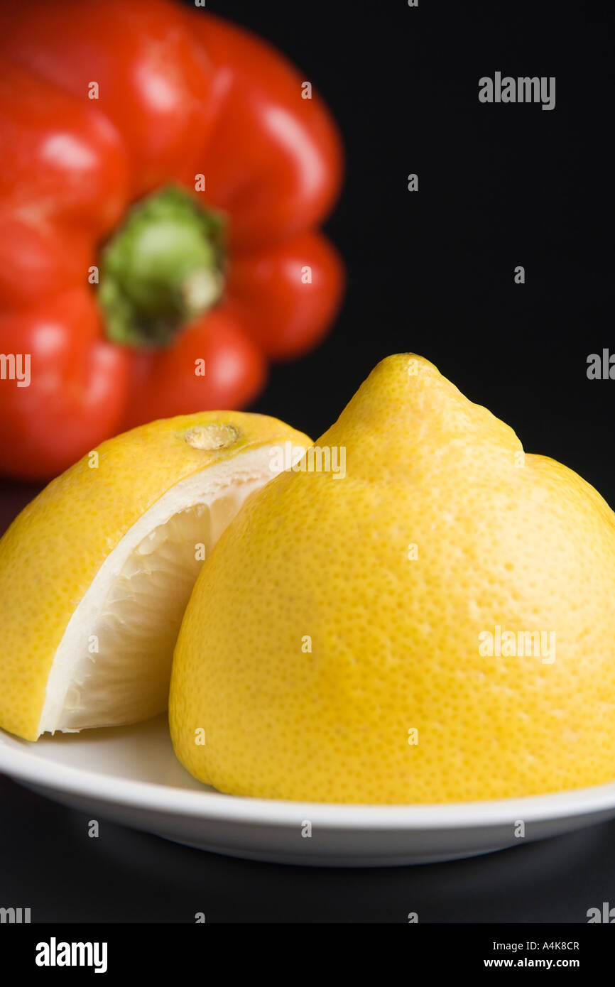 Two lemon halves in front of a red bell pepper on a dark background ...